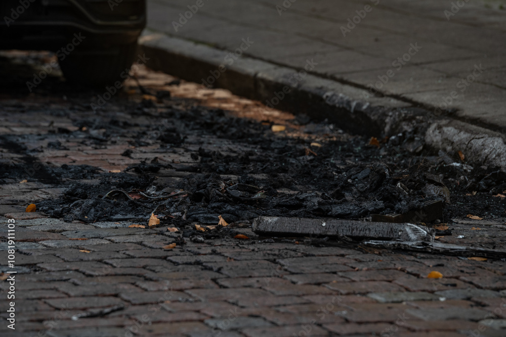 Charred remains on a cobblestone street where a car has burned. The ...