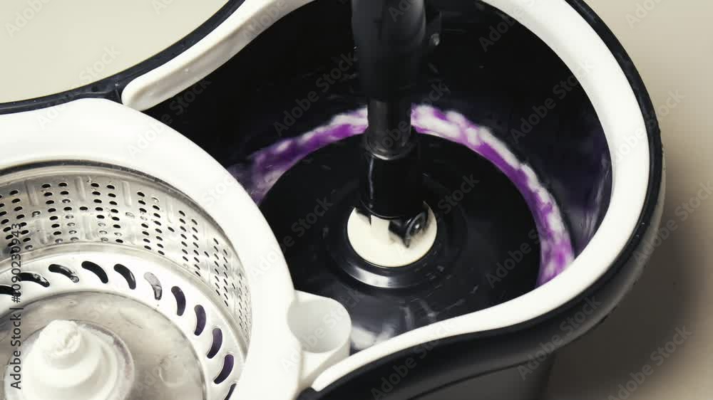 A close-up of a drying a wet mop in a spinner in a bucket, house chores ...