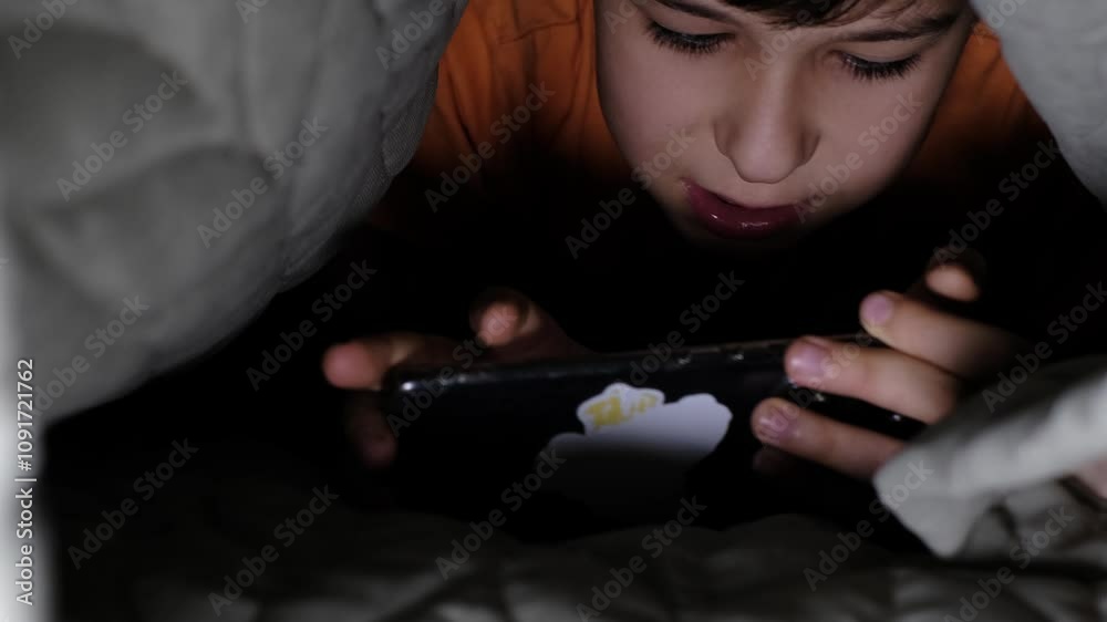 A boy plays on a smartphone under the covers late at night. The image ...