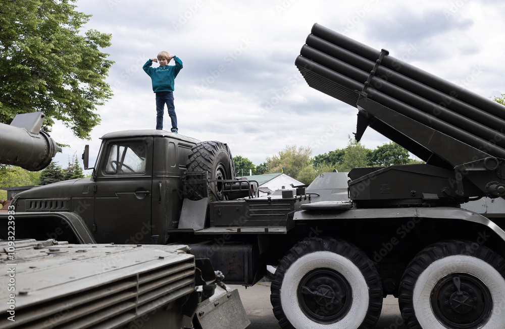 young boy stands on top of cockpit of military armored vehicle ...