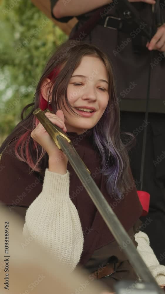 Medieval warriors talk sitting in village yard. Girl with sword smiles ...
