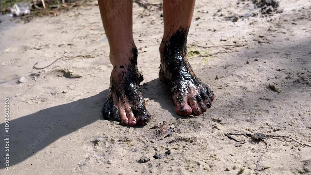 Close-up view of man's mud-caked feet on a sandy beach, highlighting ...