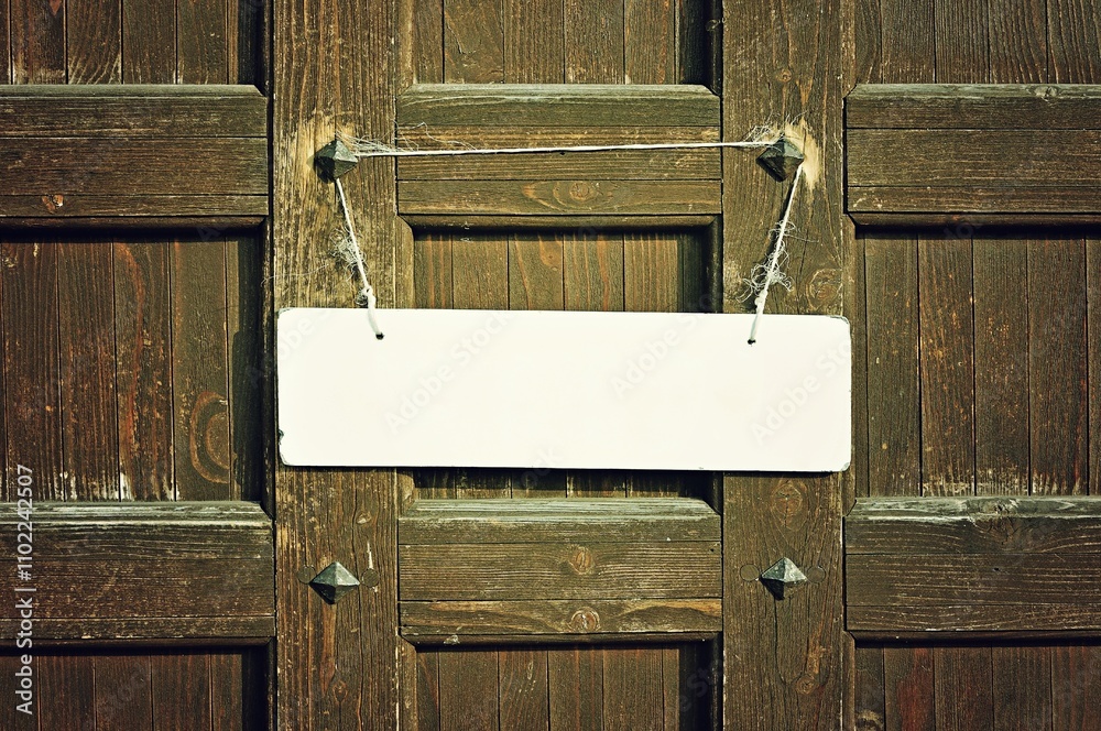 Blank white sign hanged with tattered rope on the old brown wooden door ...