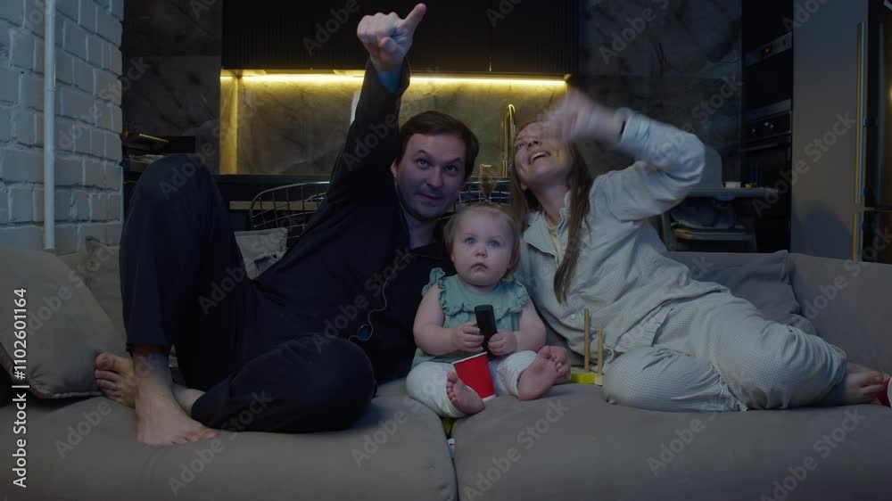 Parents are laughing while watching TV, sitting on couch with their ...