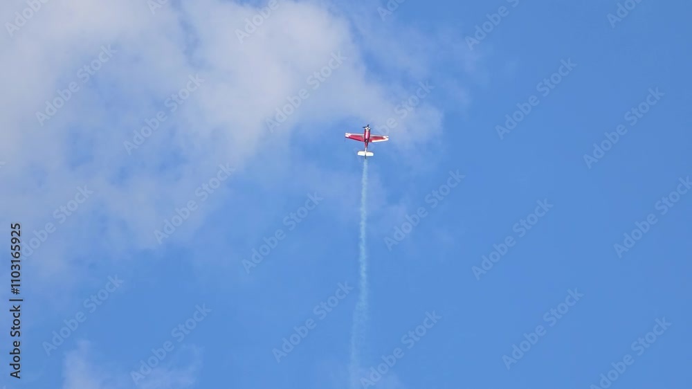 A red aerobatic plane climbs vertically while spinning, leaving a smoke ...