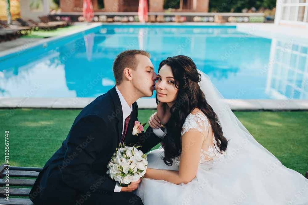 Beautiful newlyweds cuddle near the palace, sitting by the pool with ...