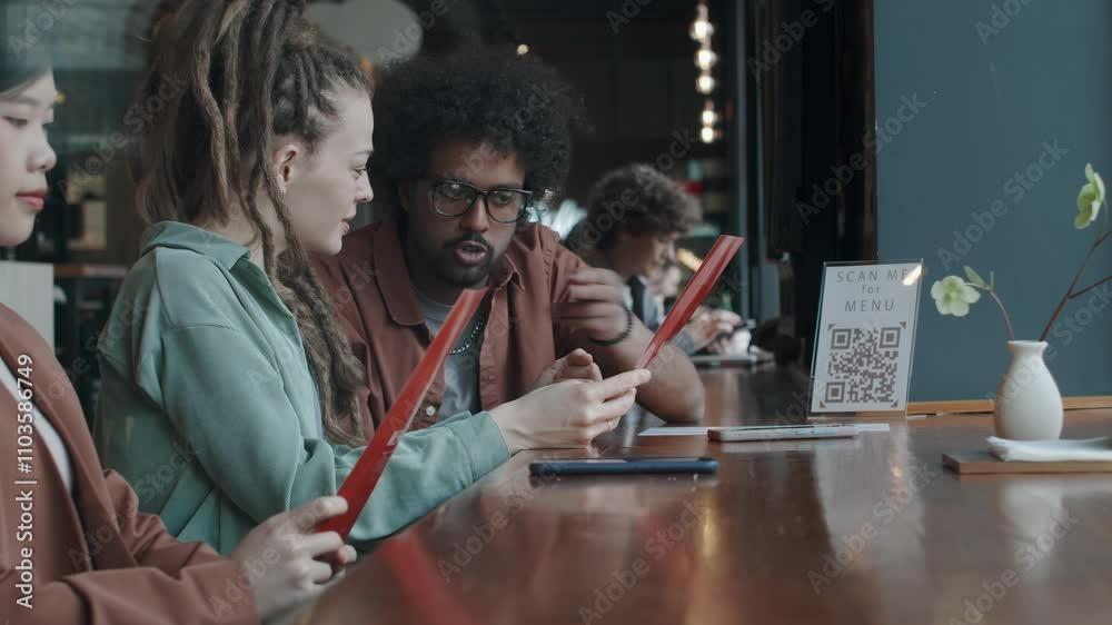 Group of three friends looking through and discussing menu sitting at ...