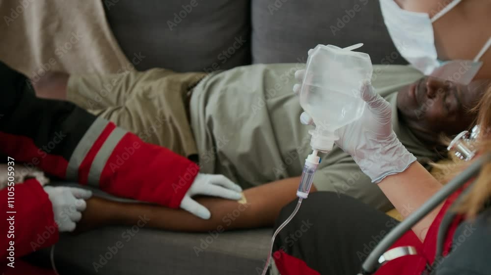 Female paramedic in protective mask and gloves holding IV bag with tube ...