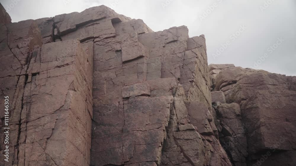 Tall angular sea cliffs with lines of erosion beneath grey skies in ...