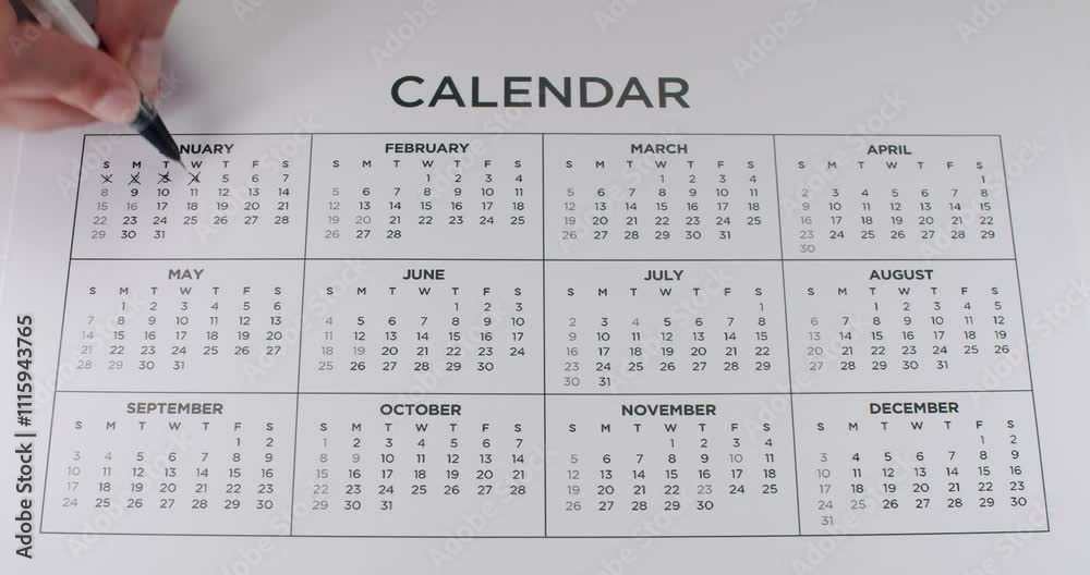 A person marks days on a yearly calendar with a pen, indicating ...