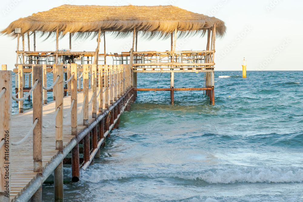 Poster A wooden hut restaurant on stilts built on the blue sea with a ...