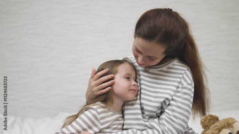 Mother calms upset little child kissing in forehead sitting on bed. Mom ...