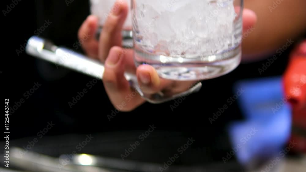 Bartender adds ice cubes into glass. slow motion, making cocktail at bar counter, Vertical ...