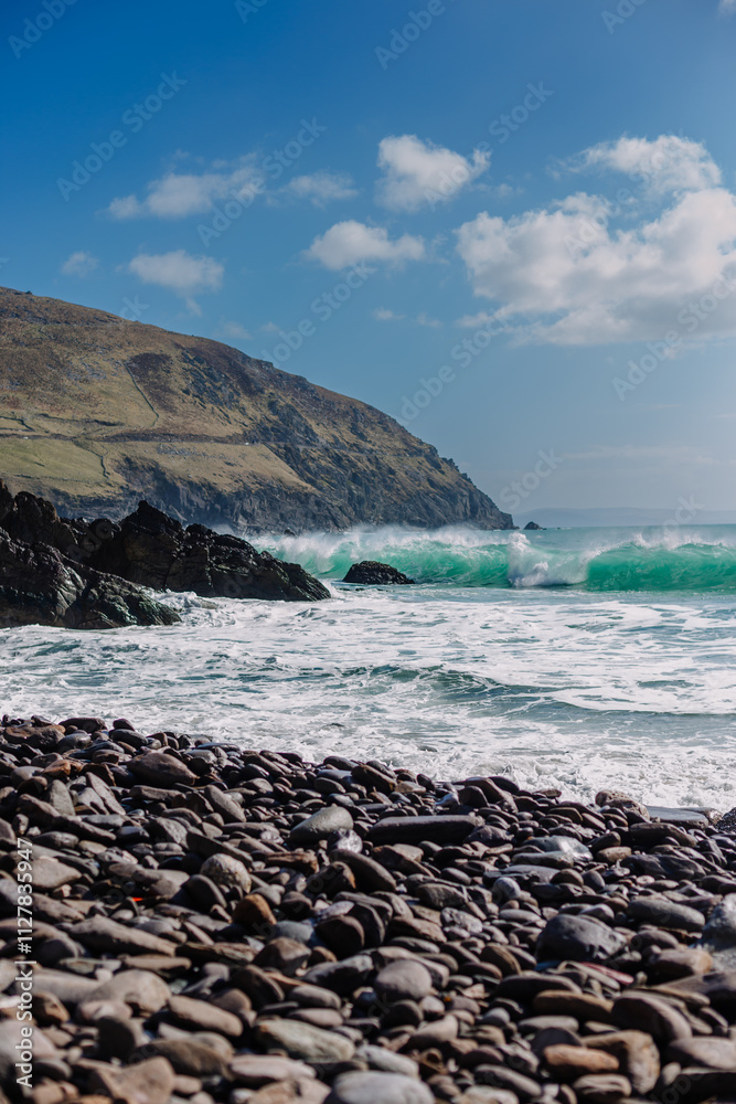 Rocky beach with smooth pebbles in the foreground. green waves crash ...