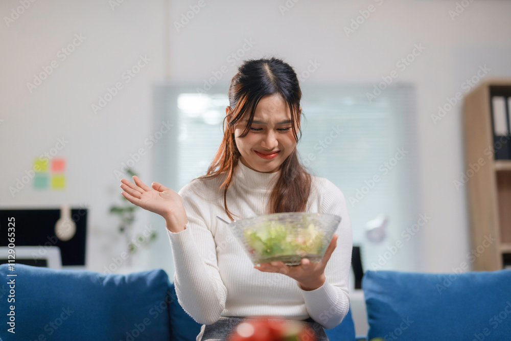 Young woman holding a bowl of salad with a disgusted expression on her ...