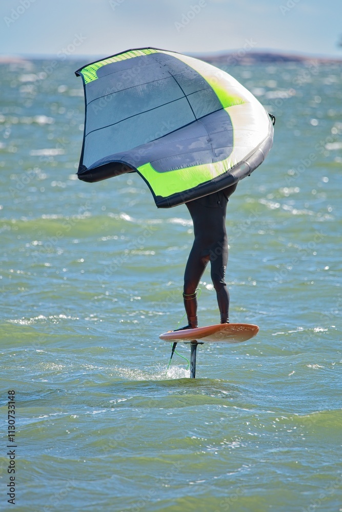Man is wing foiling using handheld inflatable wing and hydrofoil ...