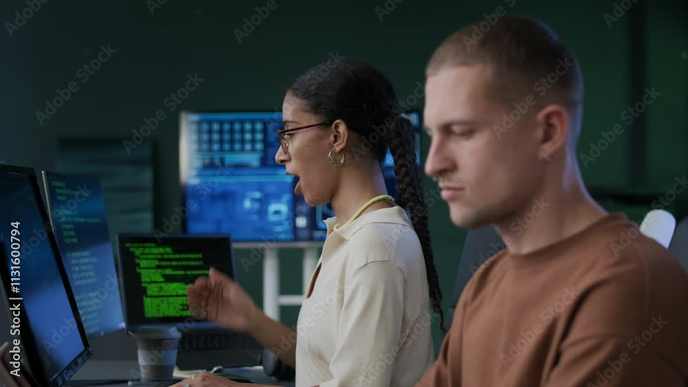 Young female biracial programmer in eyeglasses typing on PC and yawning ...