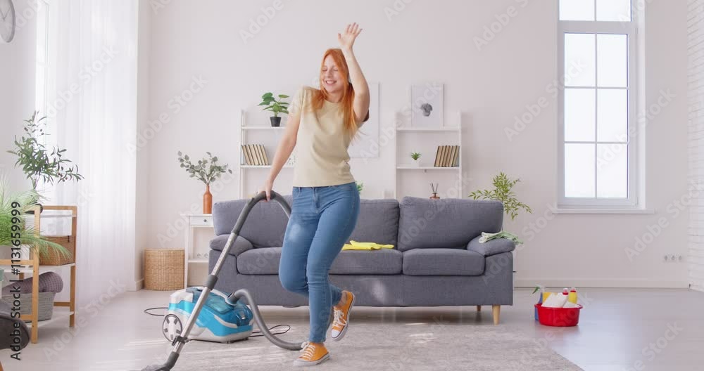 Cheerful redhead Caucasian woman dancing while vacuuming the floor at ...