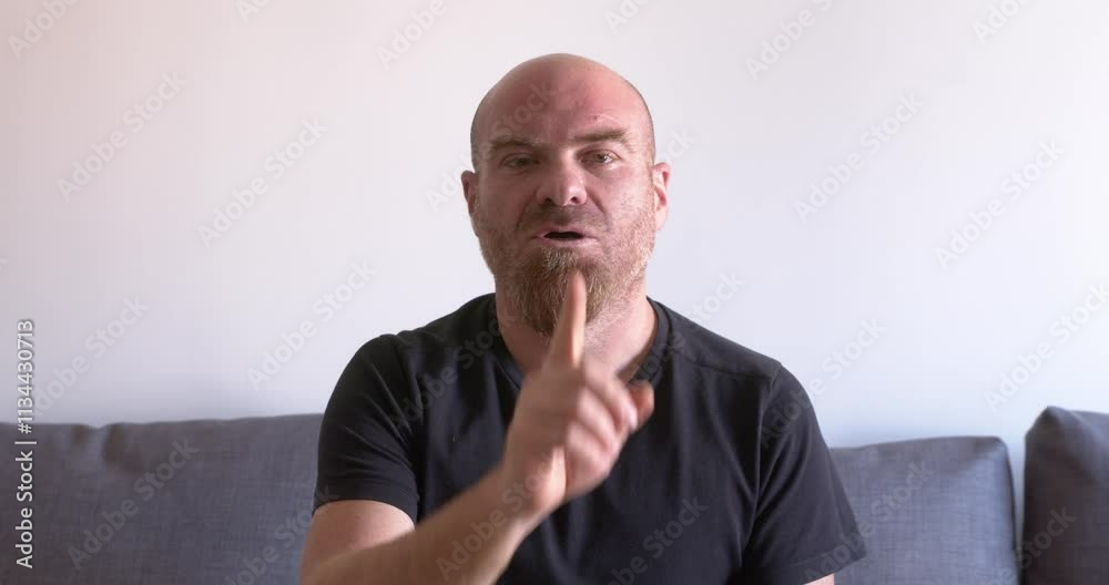 Bald man with a red goatee sitting on the couch, making a shushing ...