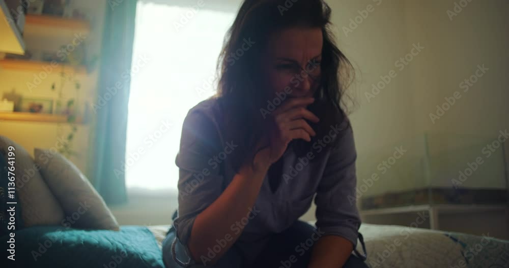 Woman sitting on a bed, crying with her head down, overwhelmed by grief ...