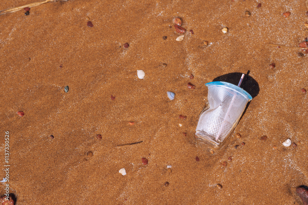 discarded plastic cup with a straw lies on a sandy beach, surrounded by ...