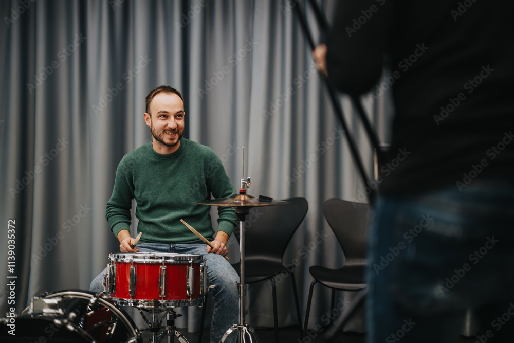 A cheerful drummer practices on his red drum set in a studio ...