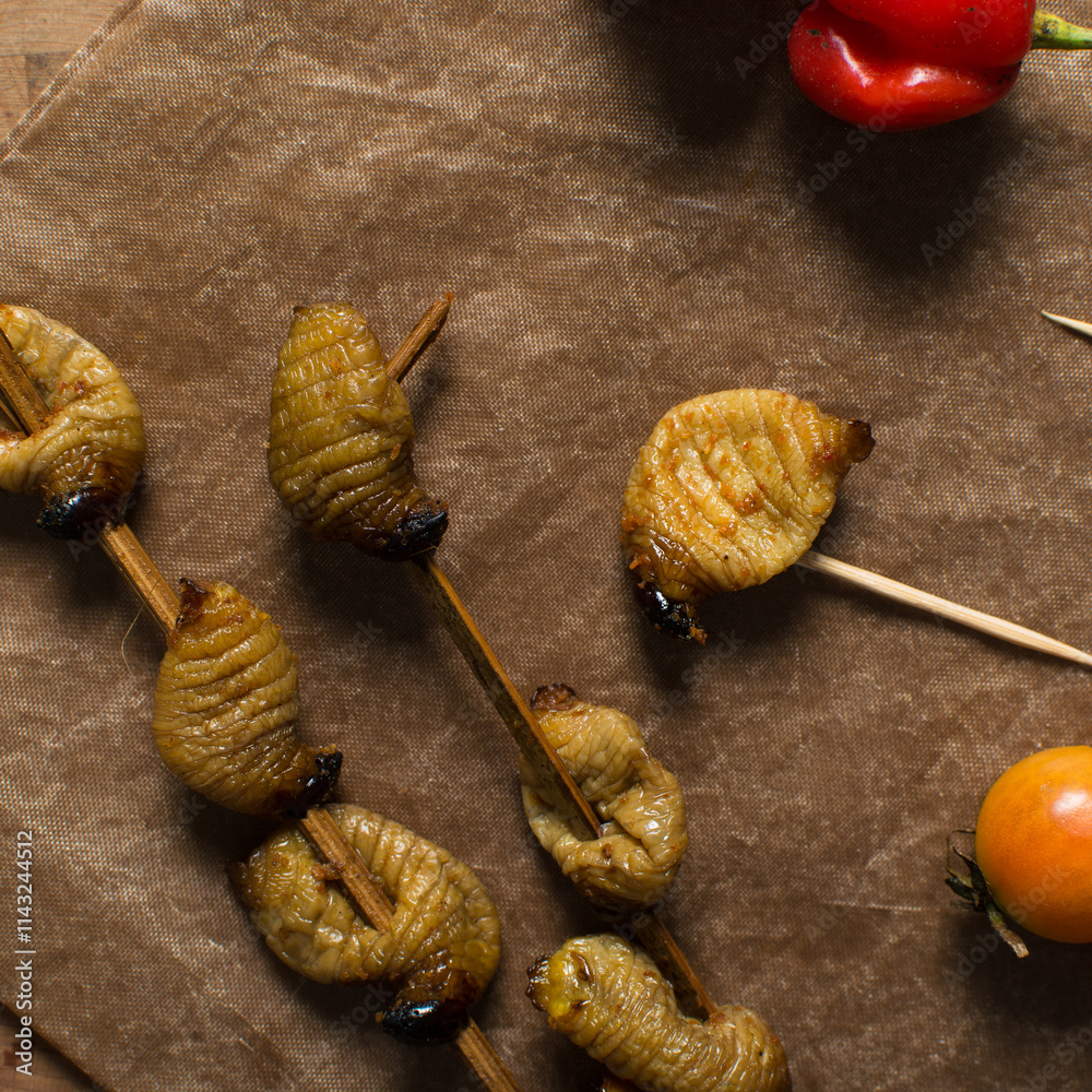 Overhead view of roasted sago worms on a wood chopping board, top view ...