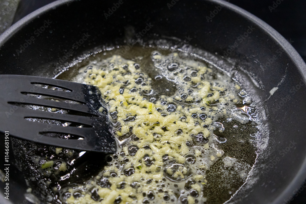 golden garlic frying in hot oil in a nonstick pan with a black spatula ...