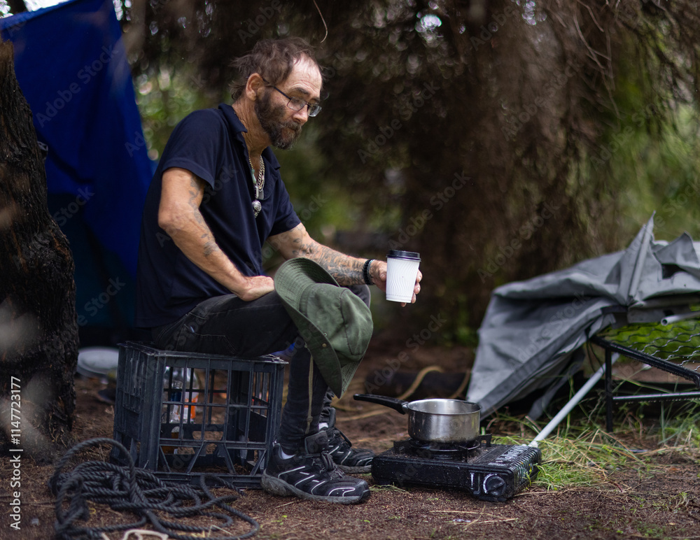 homeless man sitting on milk crate near butane stove in front of ...