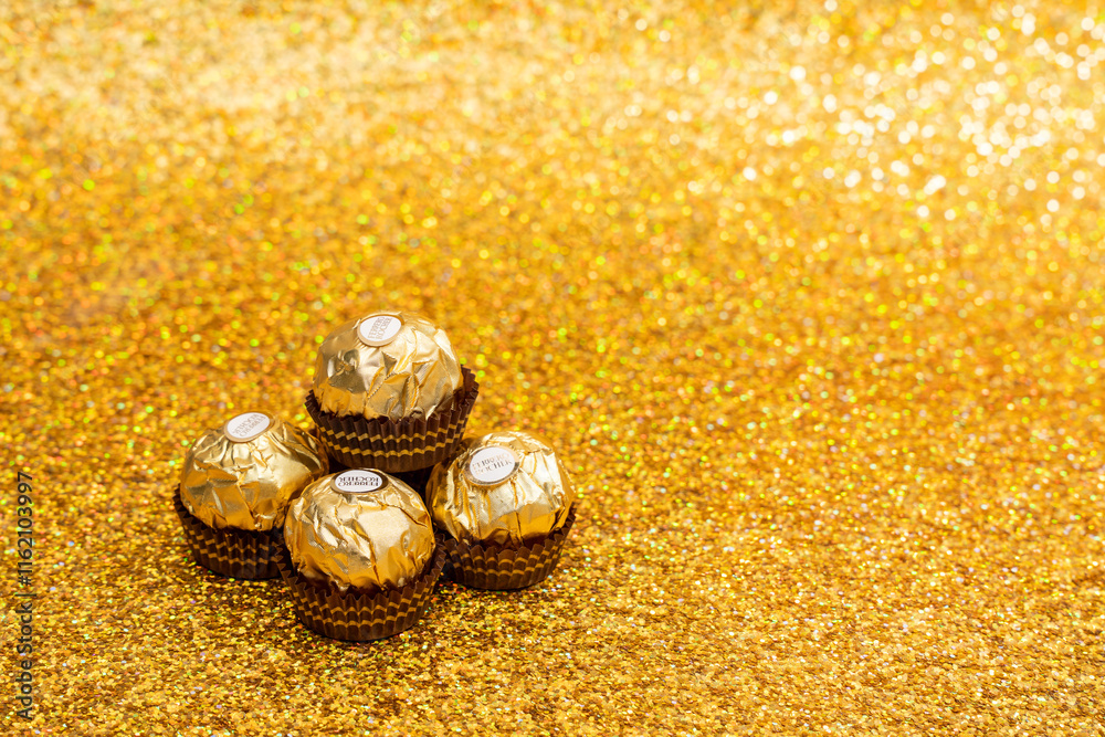 Ferrero Rocher chocolates in gold color sit on a gold background. The ...