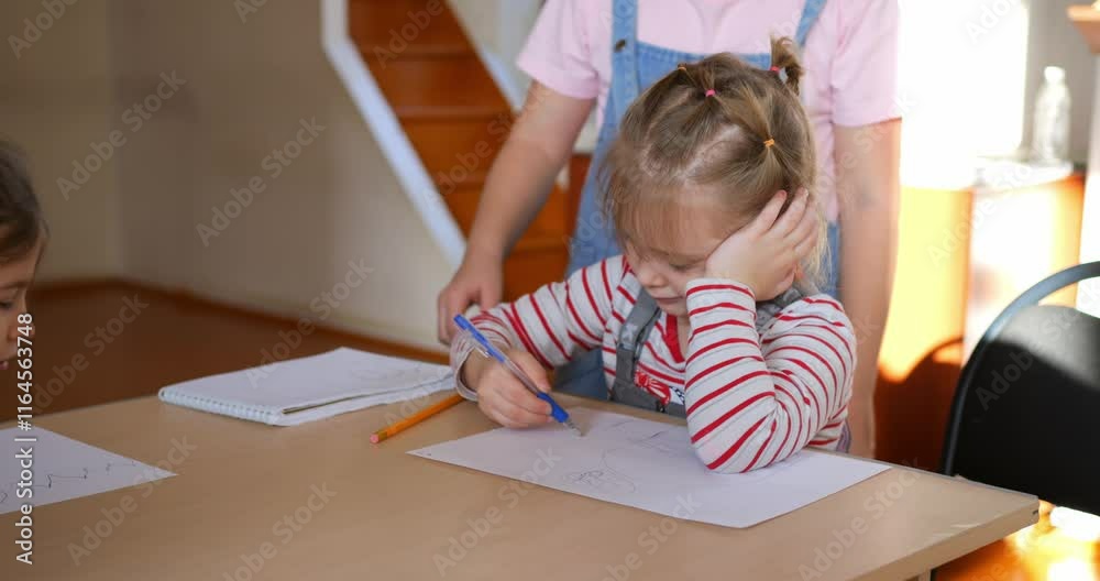 Young girl drawing intently, leaning head on hand, teacher assisting ...