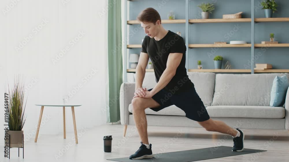 A young Caucasian man engages in a lunging exercise at home, showcasing ...