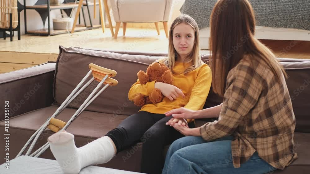 Girl with broken leg in cast sits with mother on couch at home. Sad ...