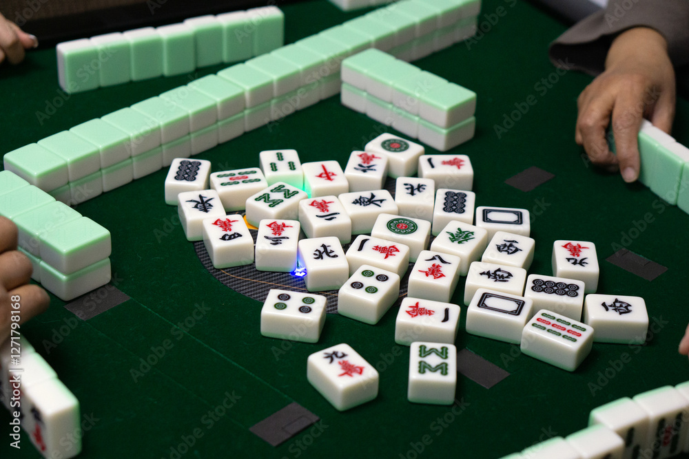Poster A game of Mahjong in full swing with hands arranging tiles on a ...