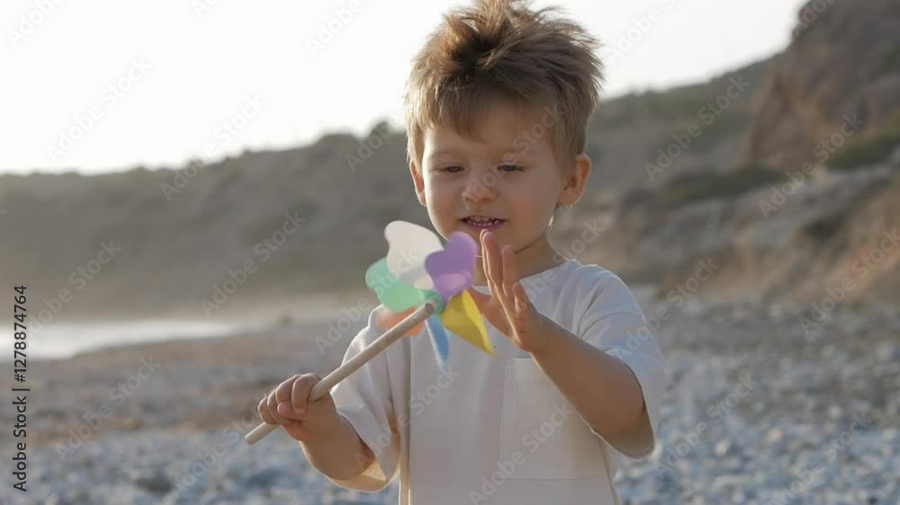 Child holds a vibrant pinwheel against a scenic ocean backdrop, feeling ...