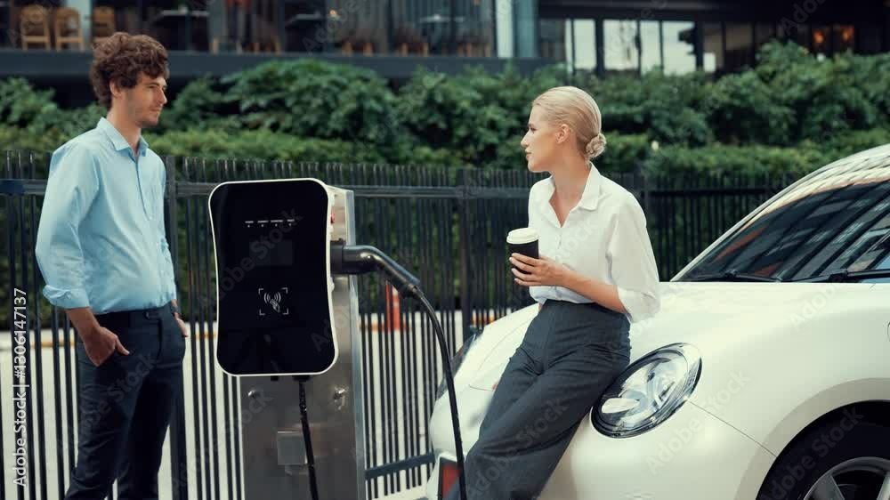 Progressive businessman and businesswoman leaning on electric car ...