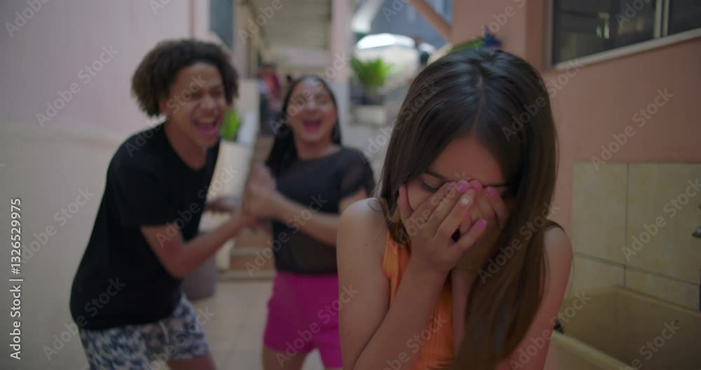 Young girl hiding face in hands while being mocked by friends in ...