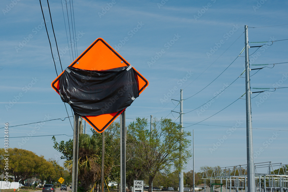 Poster Orange diamond shaped road work sign partially covered with ...