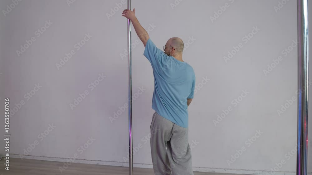 Young man, bald and masculine, walks up to pole. He jumps onto it with ...