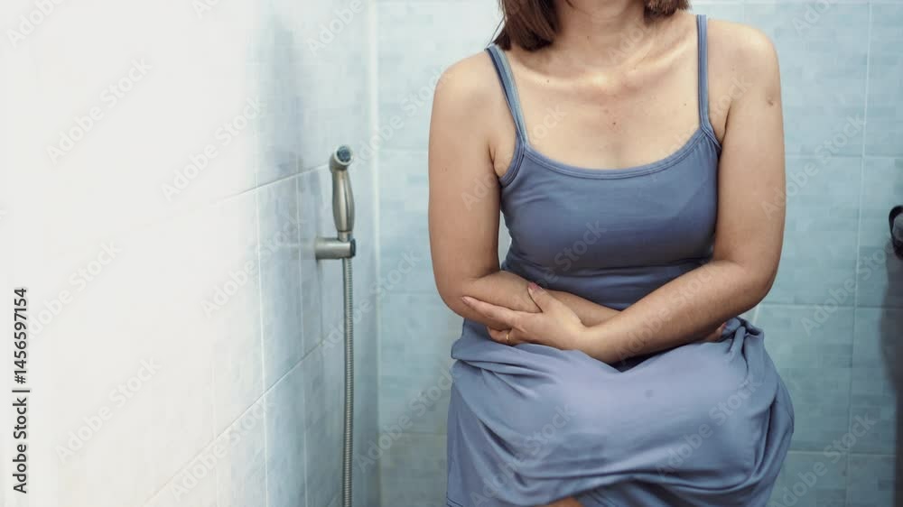 asian woman sitting on the toilet with stomach pain and cramps ...