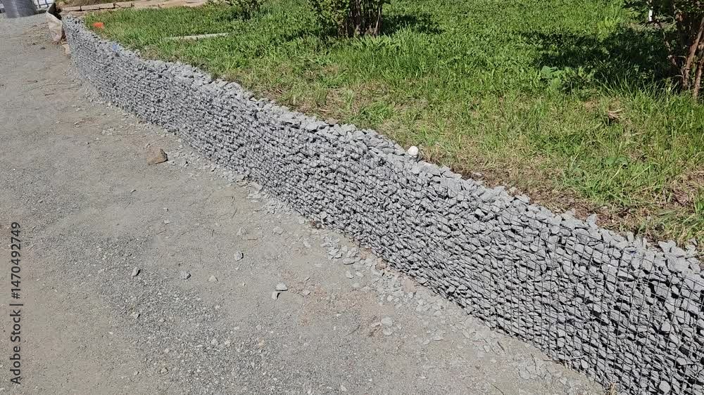 Stone gabion wall reinforcing garden edge. Wire mesh structure filled ...