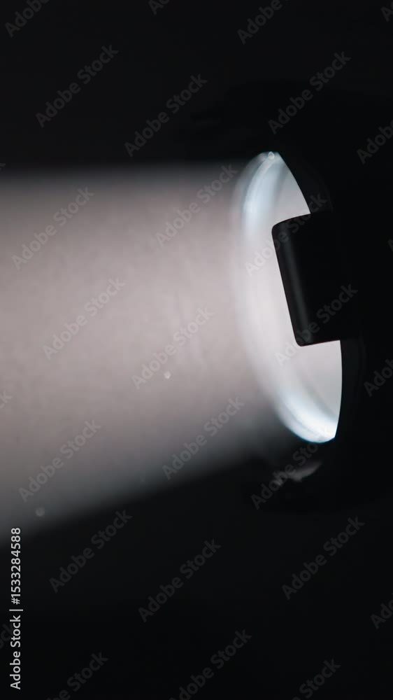 A focused beam of light from a handheld flashlight illuminates a dark ...