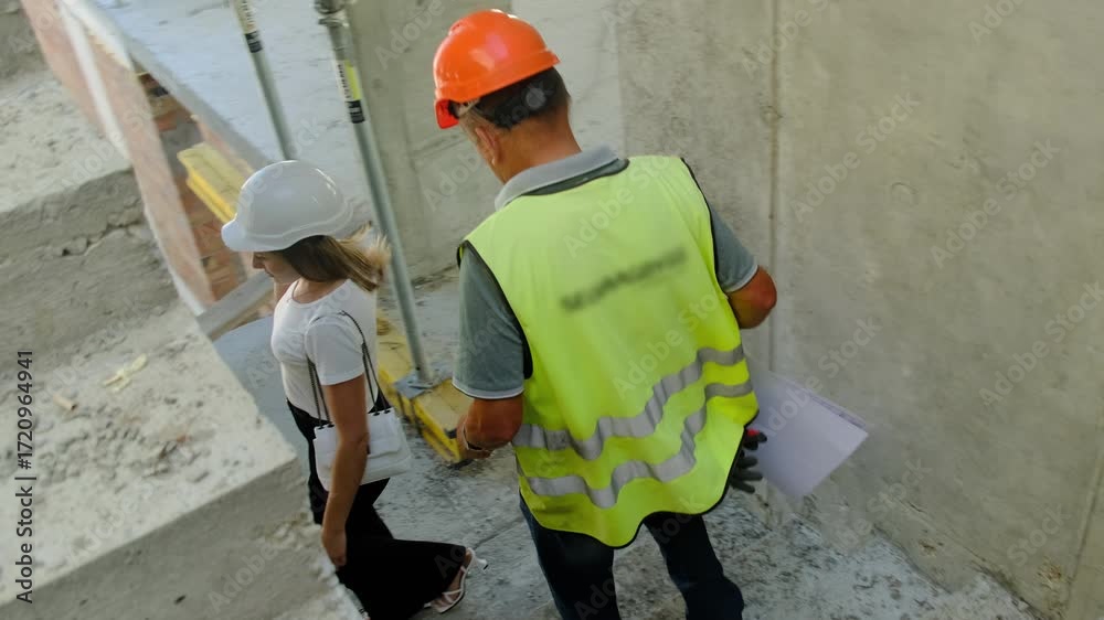 Lady expert and builder walk down steps of building. Specialists in hard hats inspect site ...