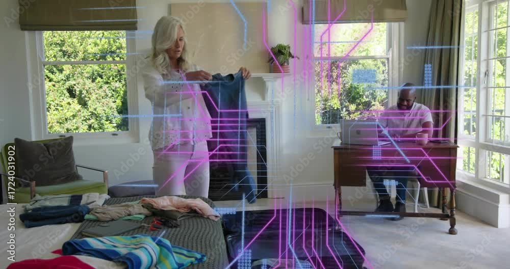 Woman unfolding garment and initiating digital overlay, couple packing ...