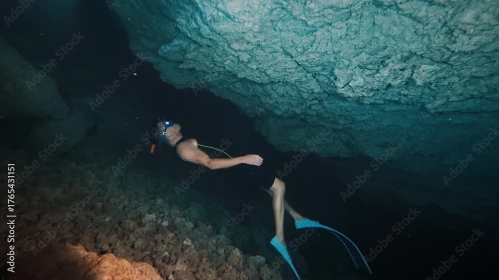 Cave freediving. Male freediver swims underwater from the dark cave and ...