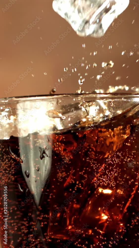 Ice cubes fall into a glass with cola. Filmed is slow motion 1000 fps ...