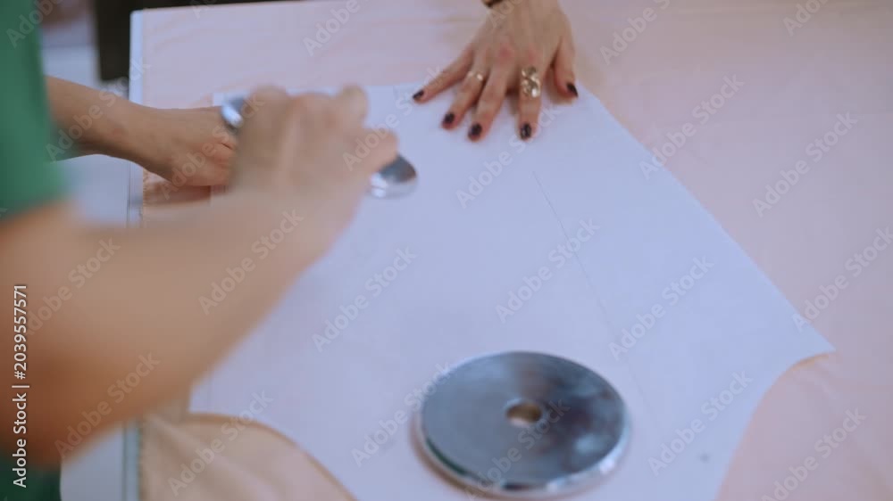 Hands of two women working with a sewing pattern and ruler on a piece ...