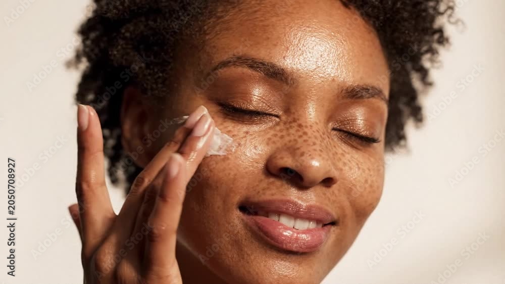Serene freckled woman applying face cream in a warm studio close-up ...