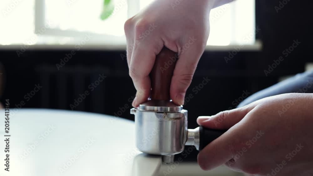 Barista tamping coffee grounds in portafilter for espresso preparation ...