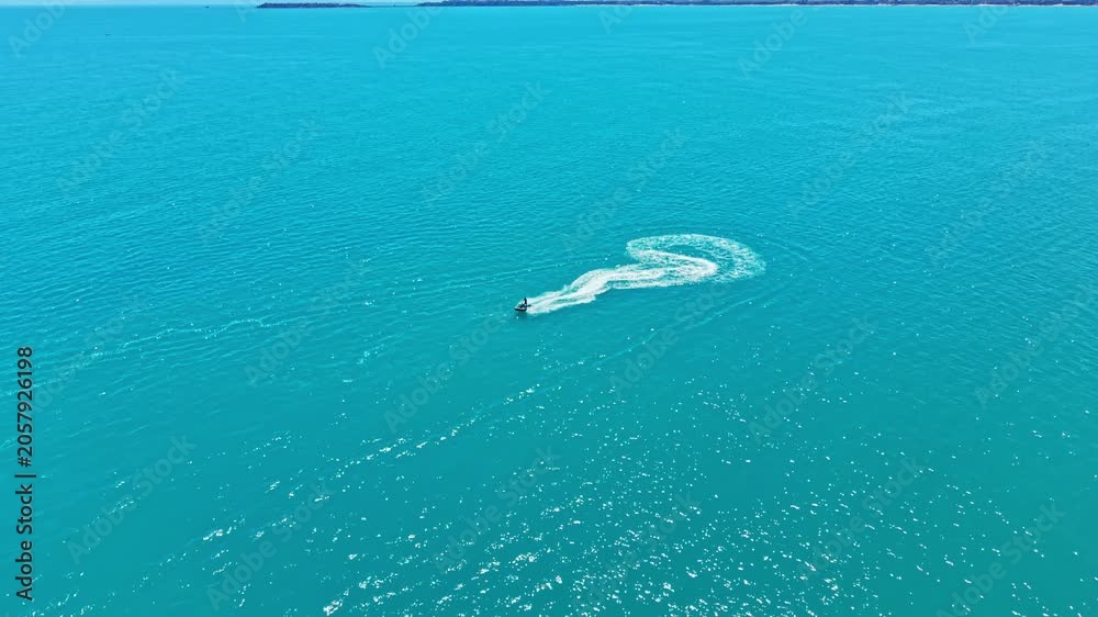 A small boat moves in a curved path on bright blue water under the ...